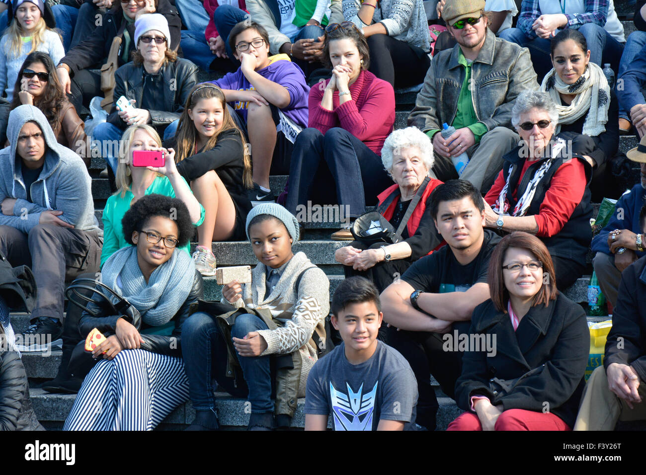 Multitude of diverse people in the USA sitting on bleachers reacting ...