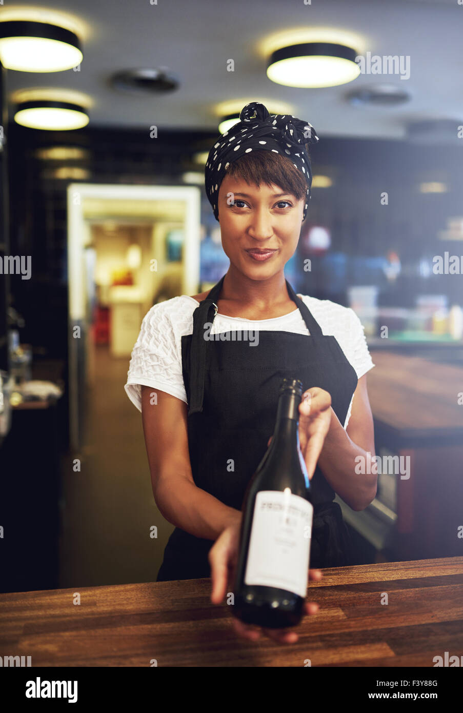 Smiling young waitress presenting a bottle of red wine to a customer ...