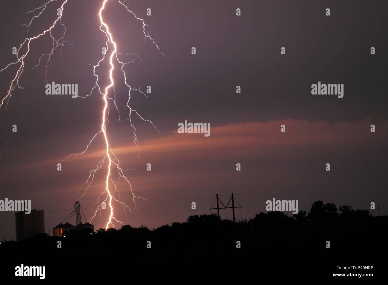 Powerful vertical bolt of lightning illuminates the sky in a purplish ...