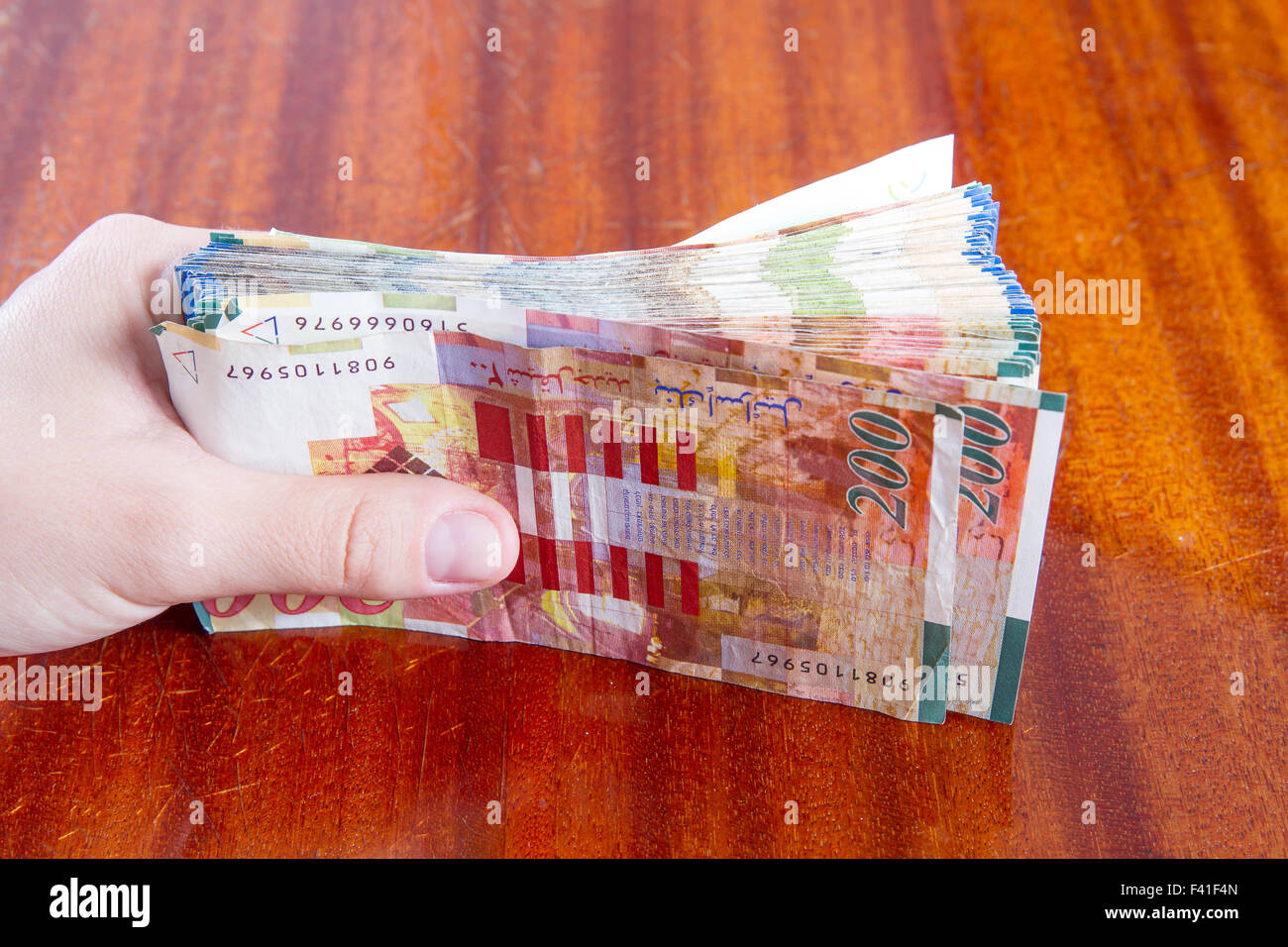 A female hand holding two hundred shekel bank notes against wood ...