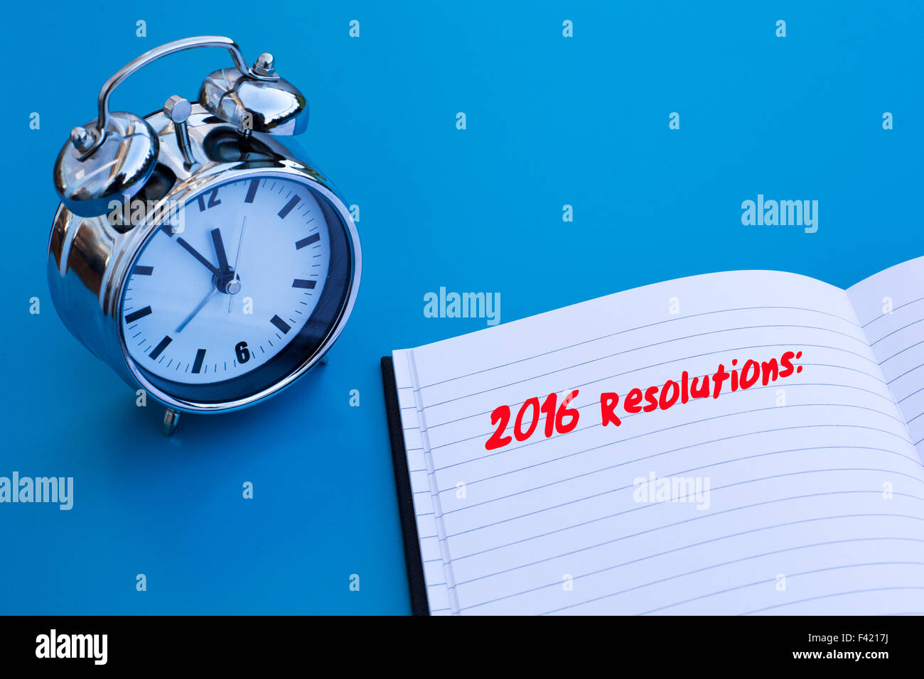 alarm clock on blue table with notepad '2016 Resoluitions' Stock Photo ...