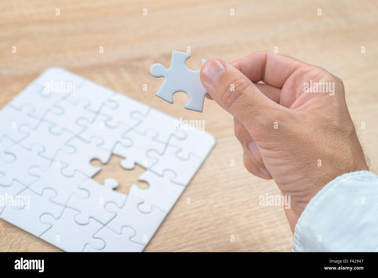 Businessman hand putting a missing piece and solving blank white jigsaw ...