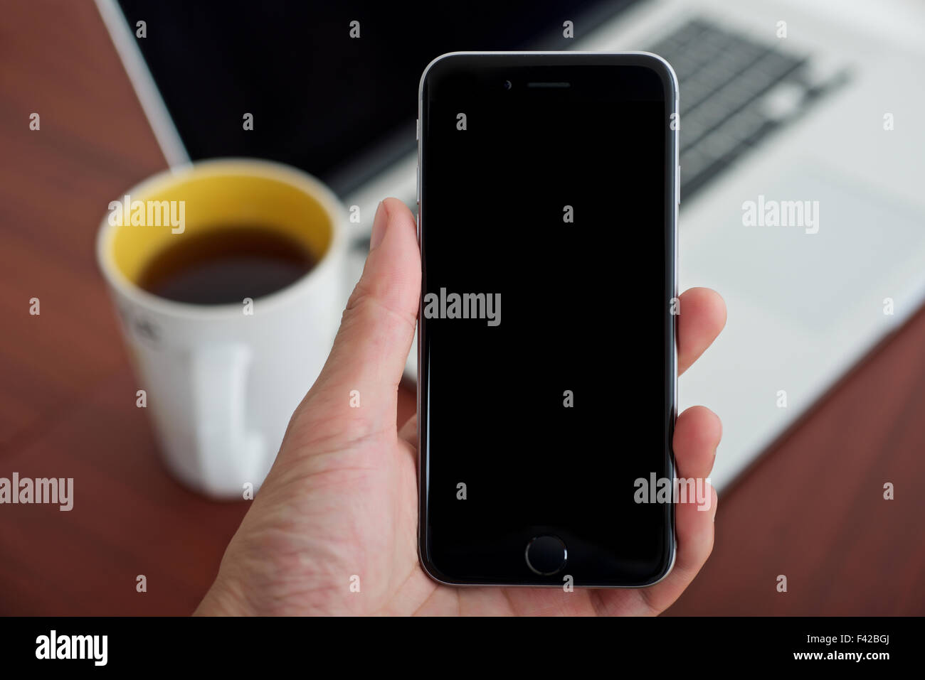 Hand holding mobile phone with wooden coffee table with laptop ...
