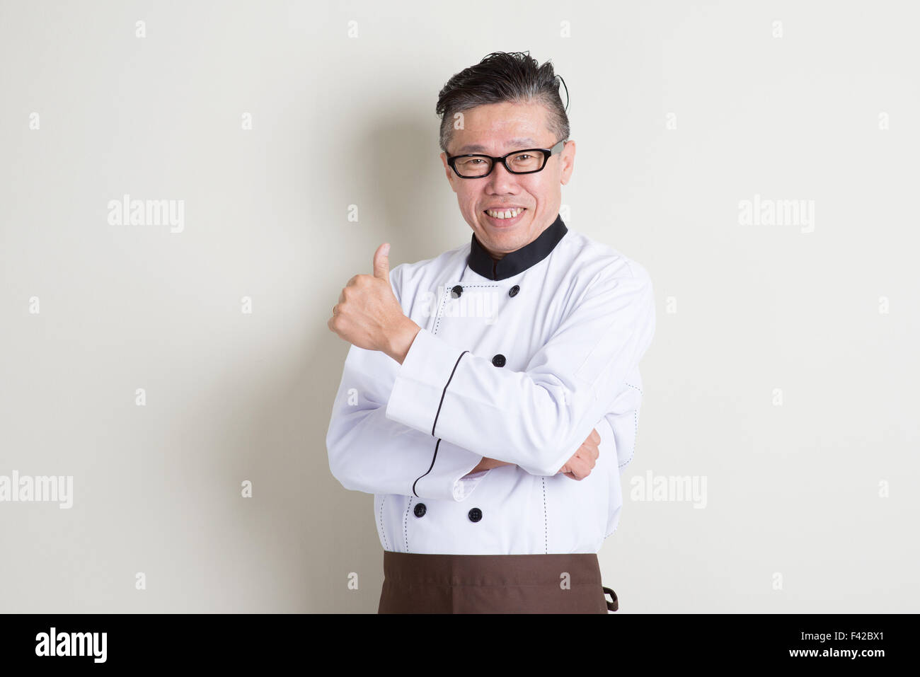 Portrait of confident 50s mature Asian male chef in uniform arms ...