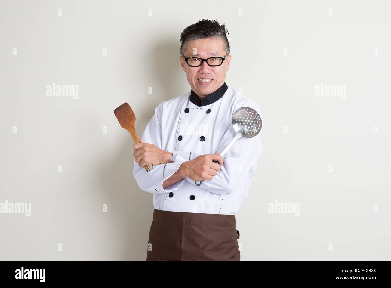 Portrait of confident 50s mature Asian male chef in uniform hands ...