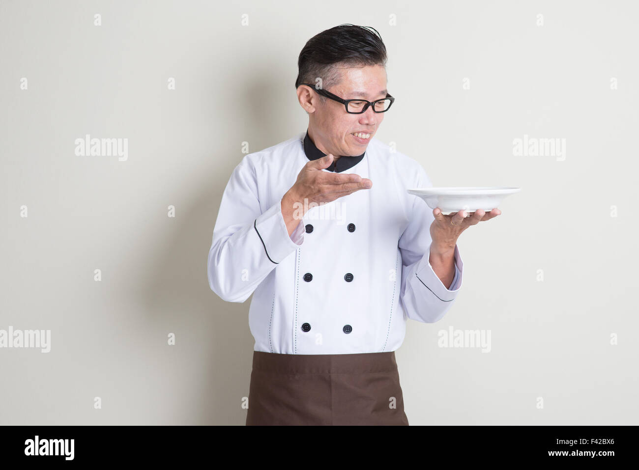 Portrait of 50s mature Asian male chef in uniform presenting his ...
