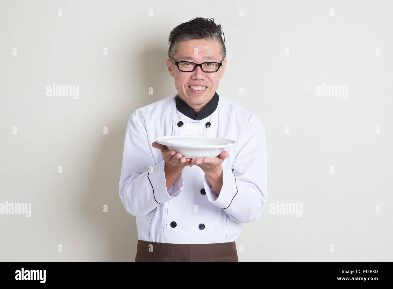 Portrait of 50s mature Asian male chef in uniform presenting dish ...