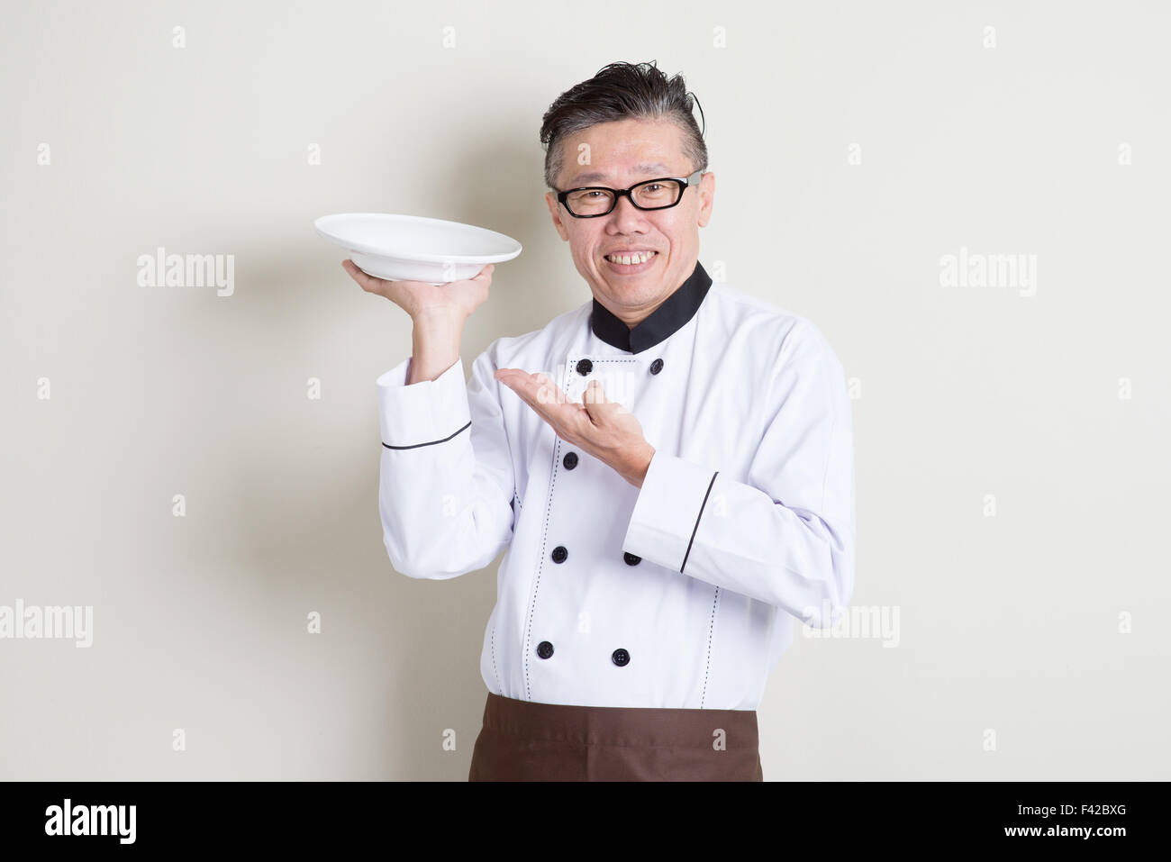 Portrait of 50s mature Asian male chef in uniform presenting dish and ...
