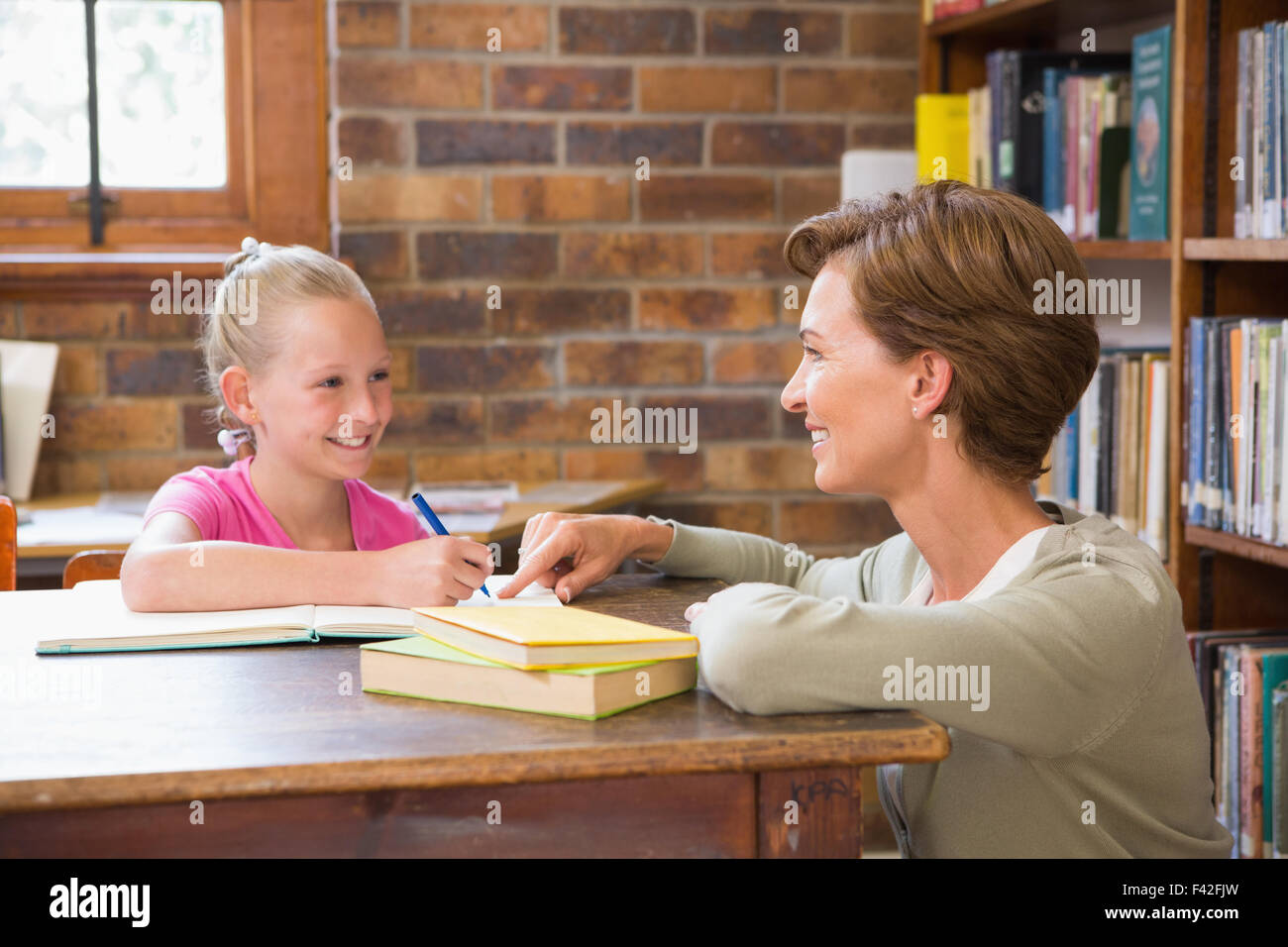 Teacher helping pupil in library Stock Photo - Alamy