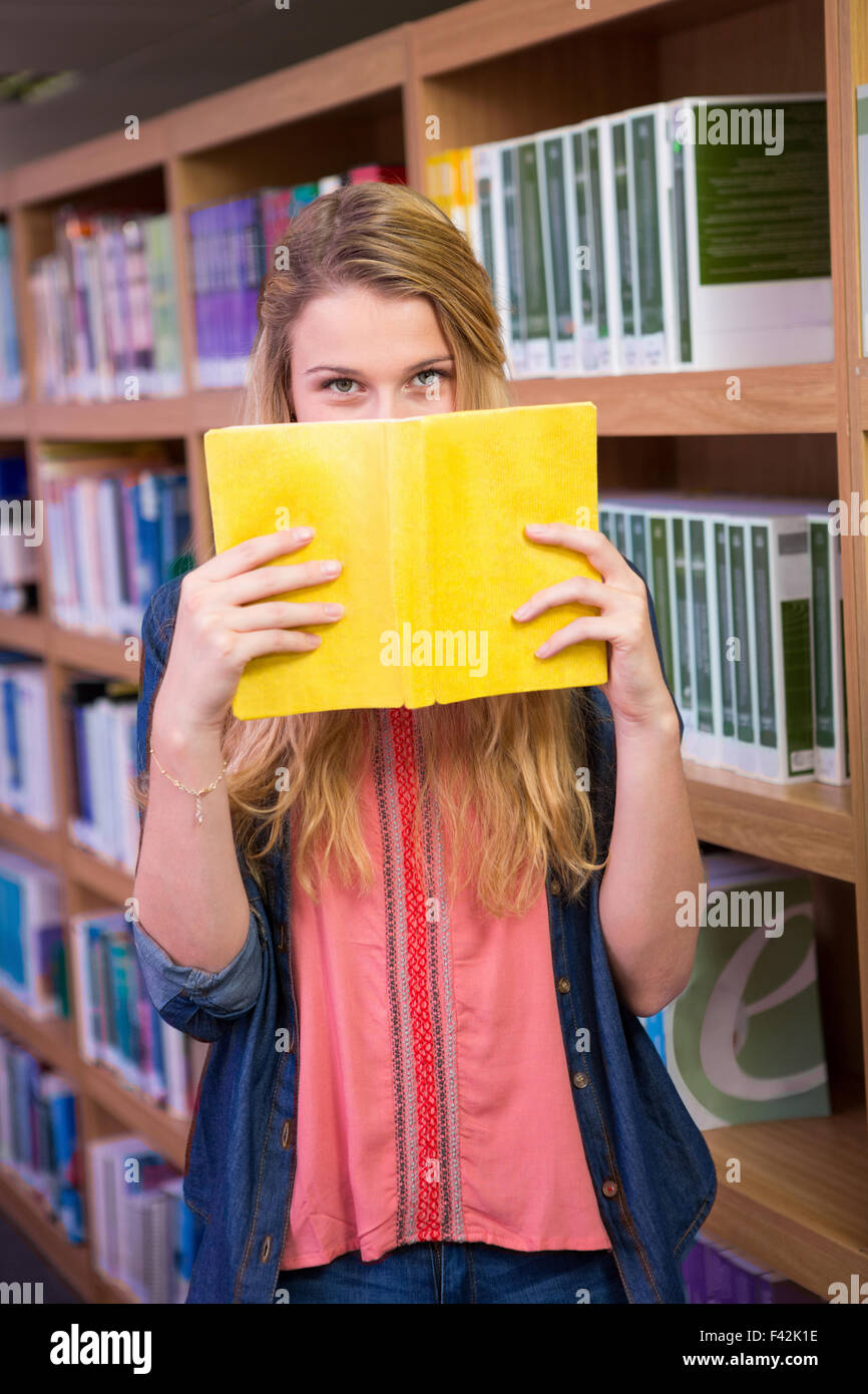 Student covering face with book in library Stock Photo - Alamy