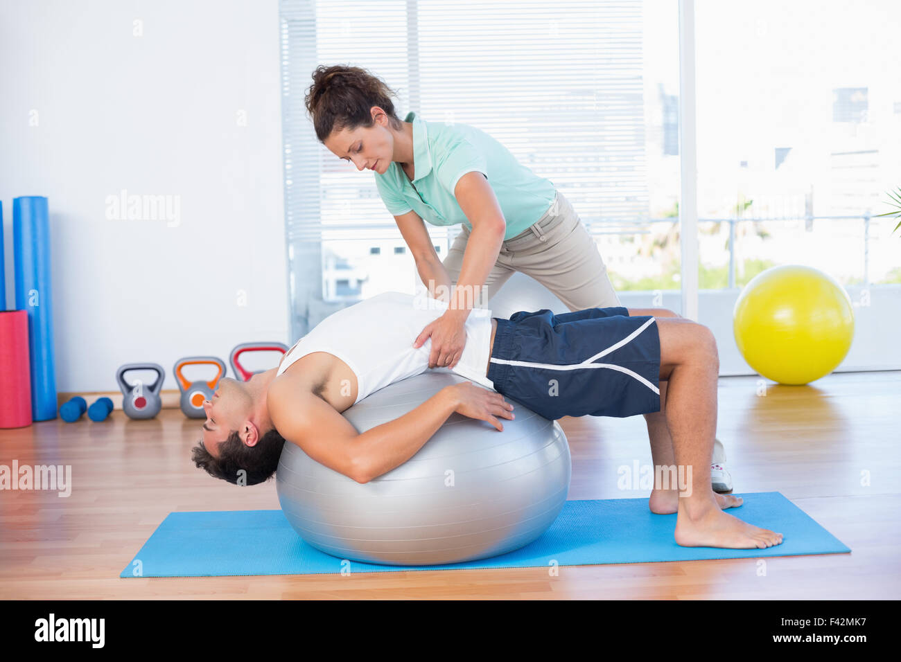 Trainer helping man with exercise ball Stock Photo - Alamy