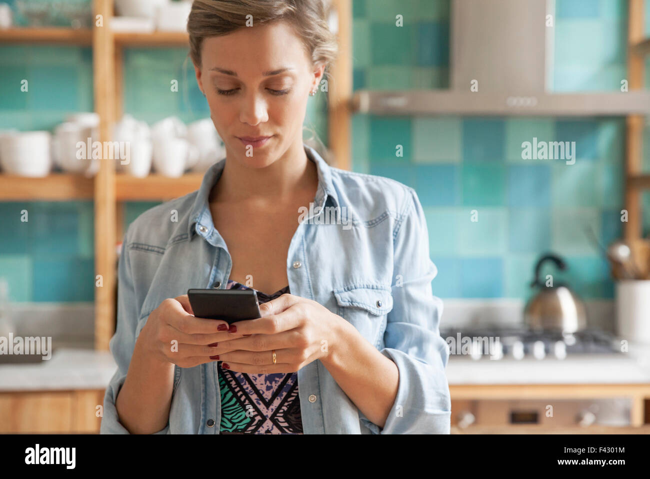 Young woman standing in kitchen with cell phone Stock Photo - Alamy