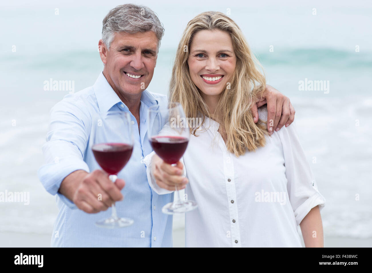 Happy couple smiling at camera and toasting Stock Photo - Alamy