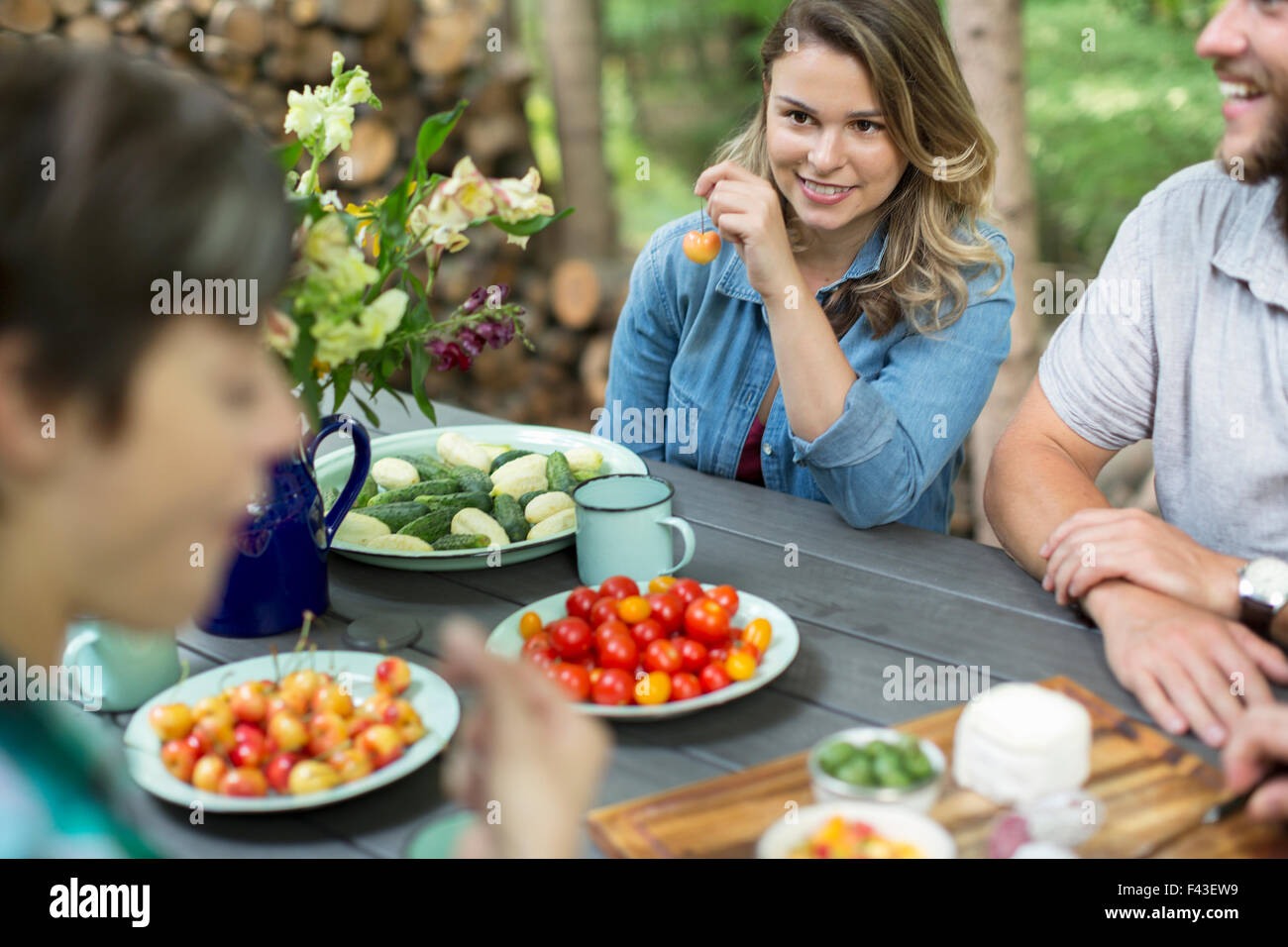 Three people seated at a table outdoors, with fresh fruit and ...