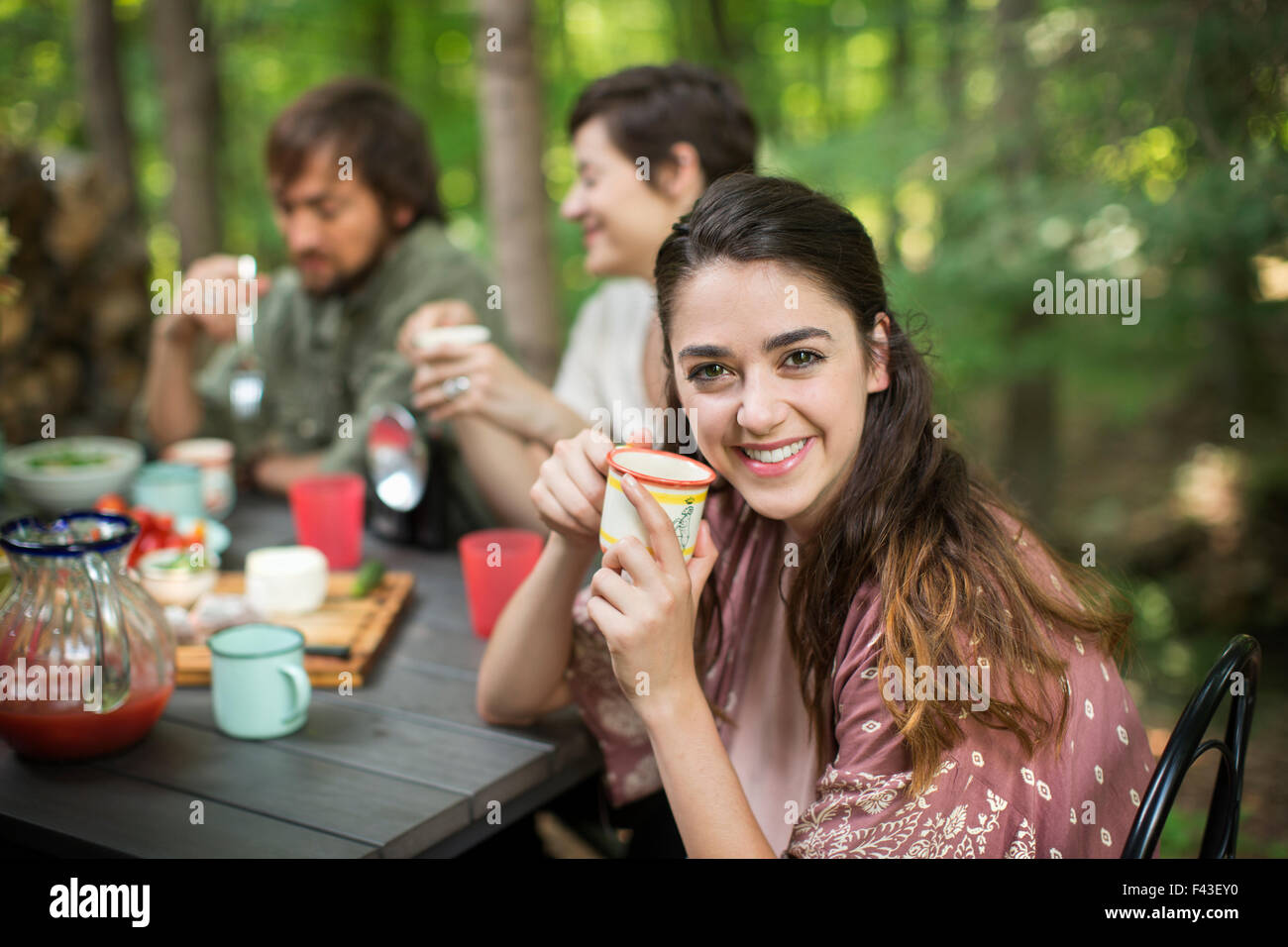 Three people seated around a table in a woodland clearing, one woman ...