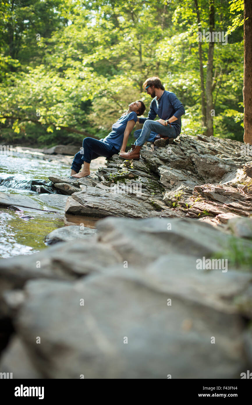 Two men seated in shade on the rocks by the river Stock Photo - Alamy