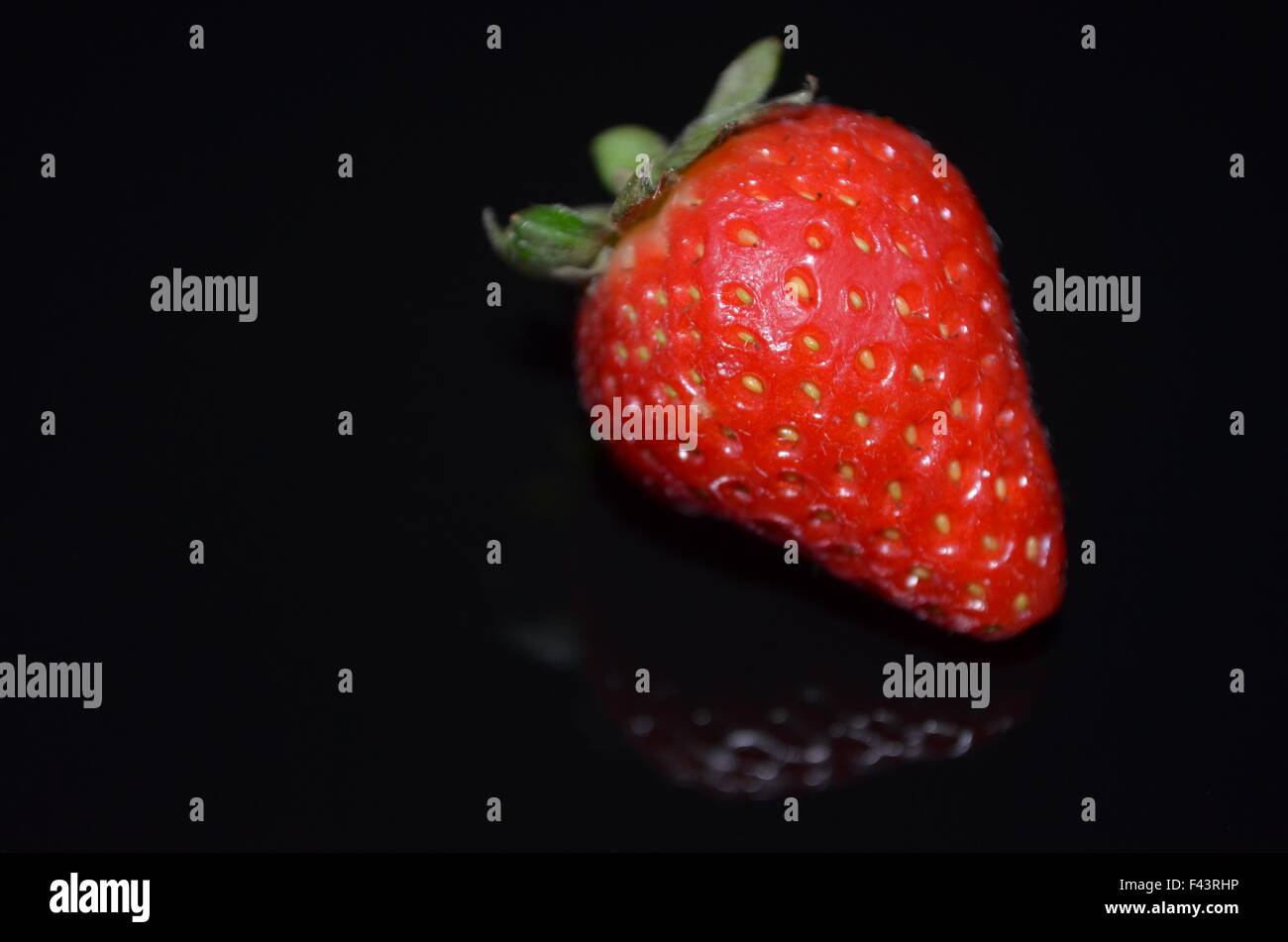 A macro shot of a red, juicy strawberry on a black reflective surface ...