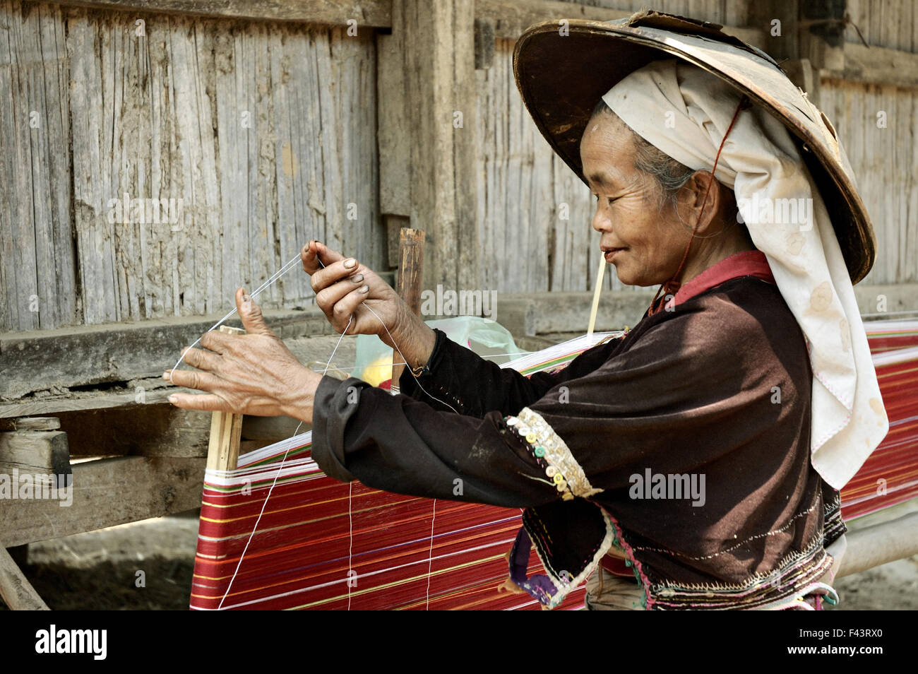 Aged Palaung woman with a conical hat weaving outside in a village ...