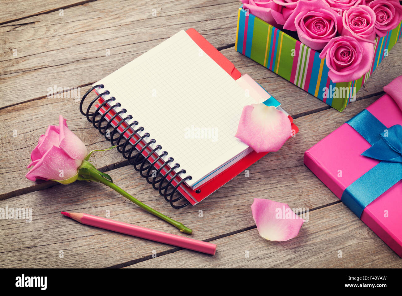 Blank notepad and gift box full of pink roses over wooden table. Top ...