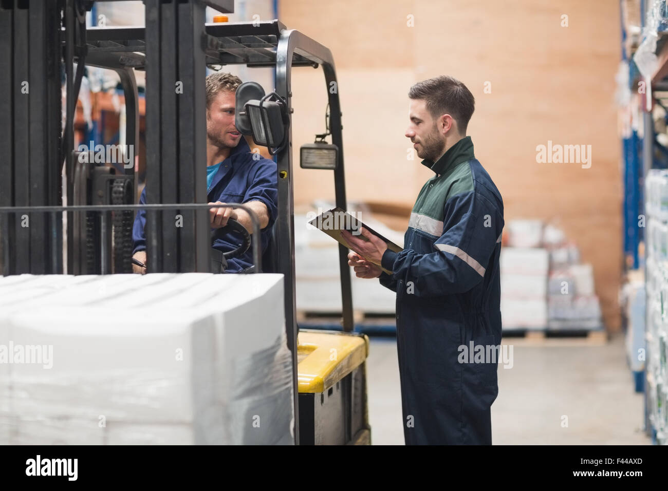 Warehouse worker talking with forklift driver Stock Photo - Alamy