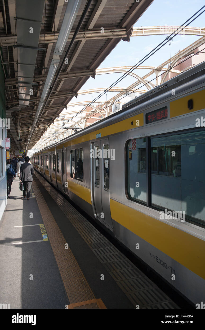 Train platform with yellow stripe train and peopl walking away business ...