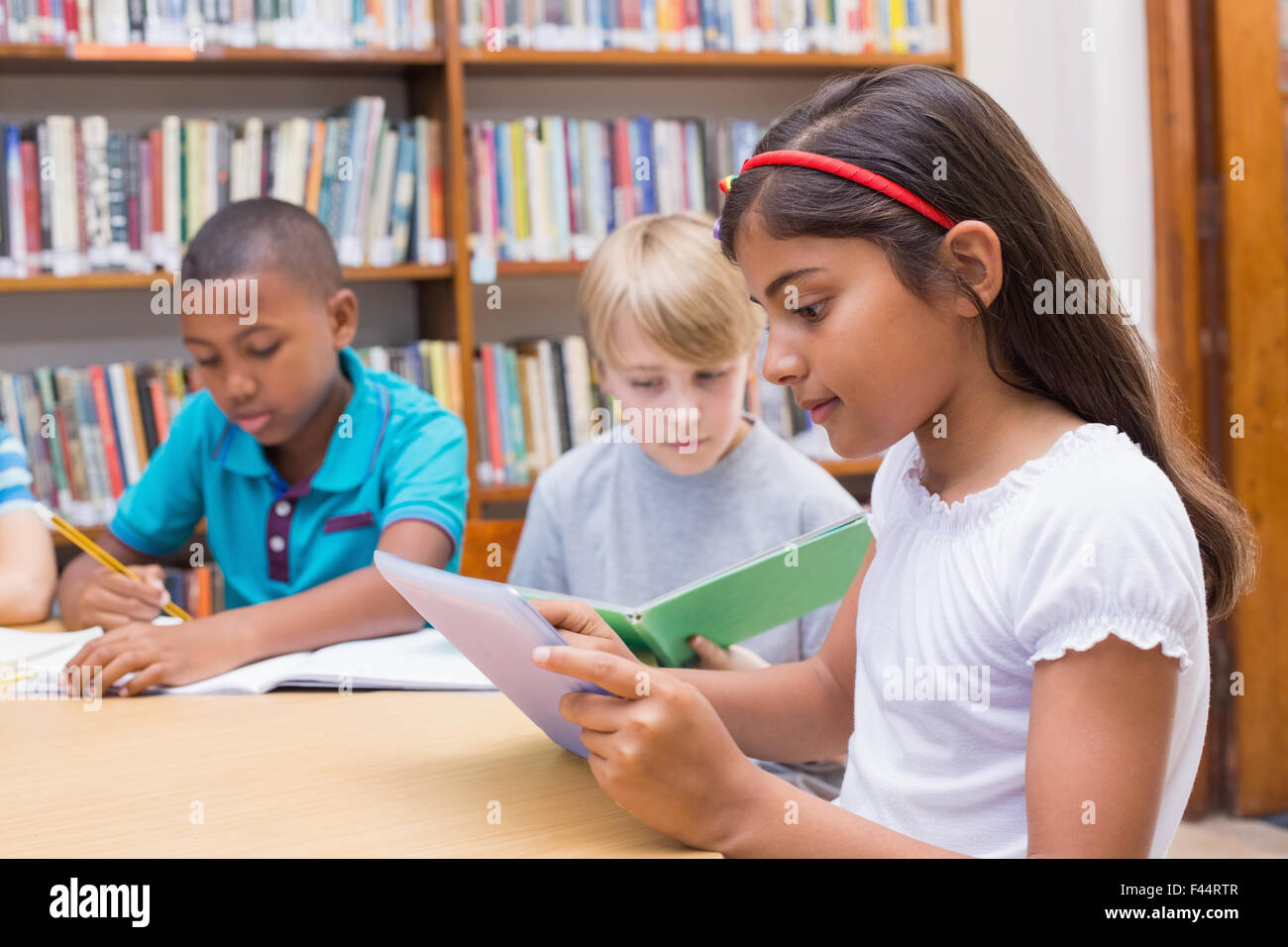 Cute pupils writing at desk in library Stock Photo - Alamy