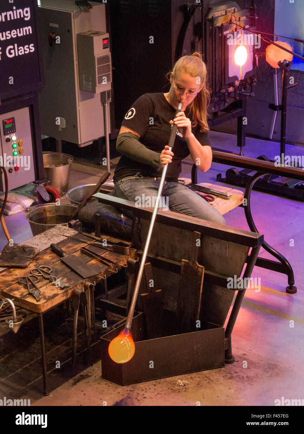 Blowing through a metal pipe, a glassblower or gaffer shapes molten ...