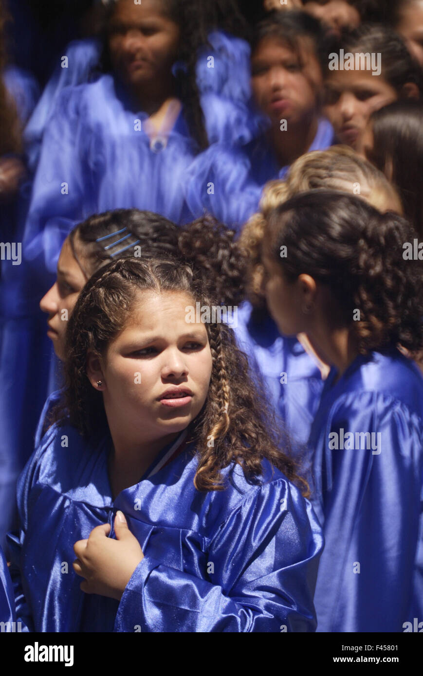 Hispanic middle school girls wearing blue graduation gowns await ...