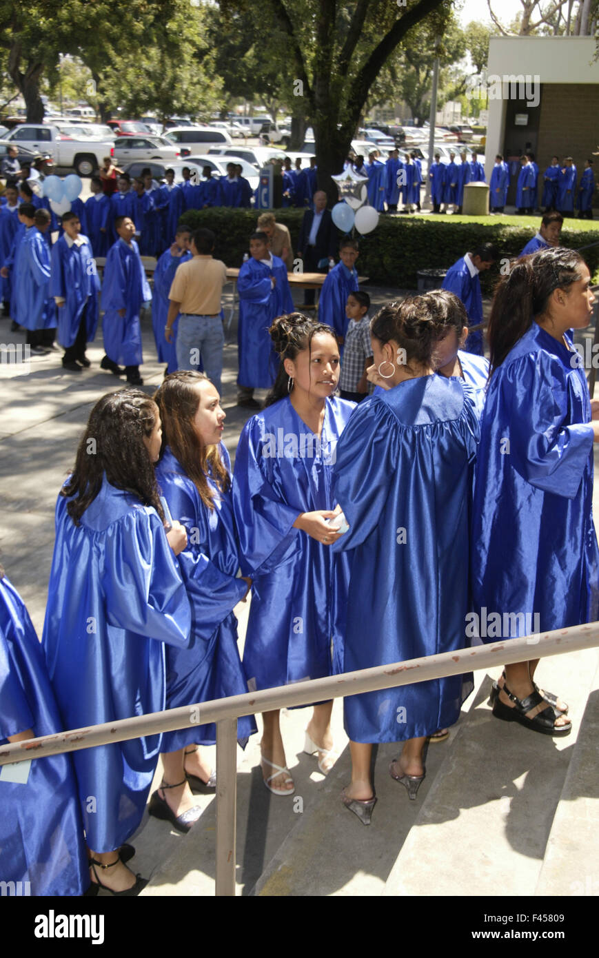 Hispanic middle school girls wearing blue graduation gowns await ...