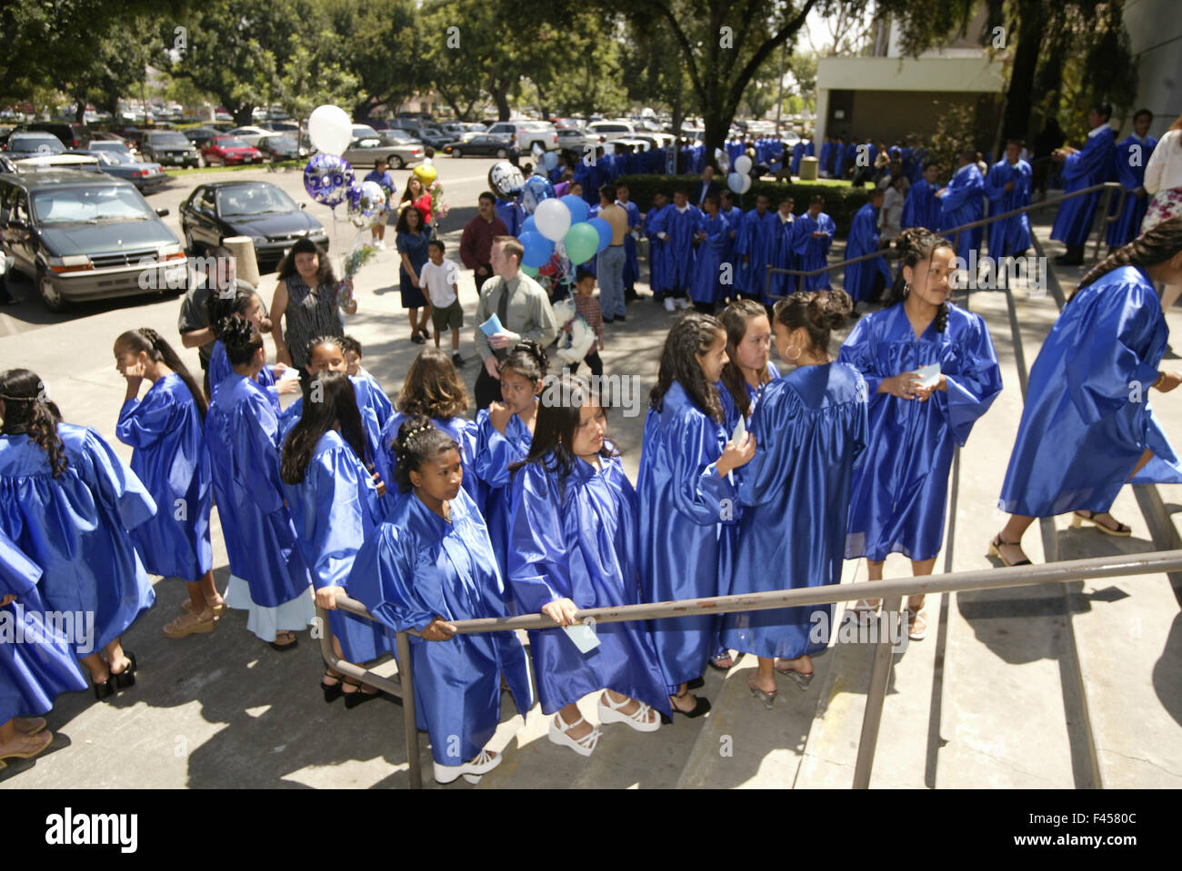 Hispanic middle school girls wearing blue graduation gowns await ...