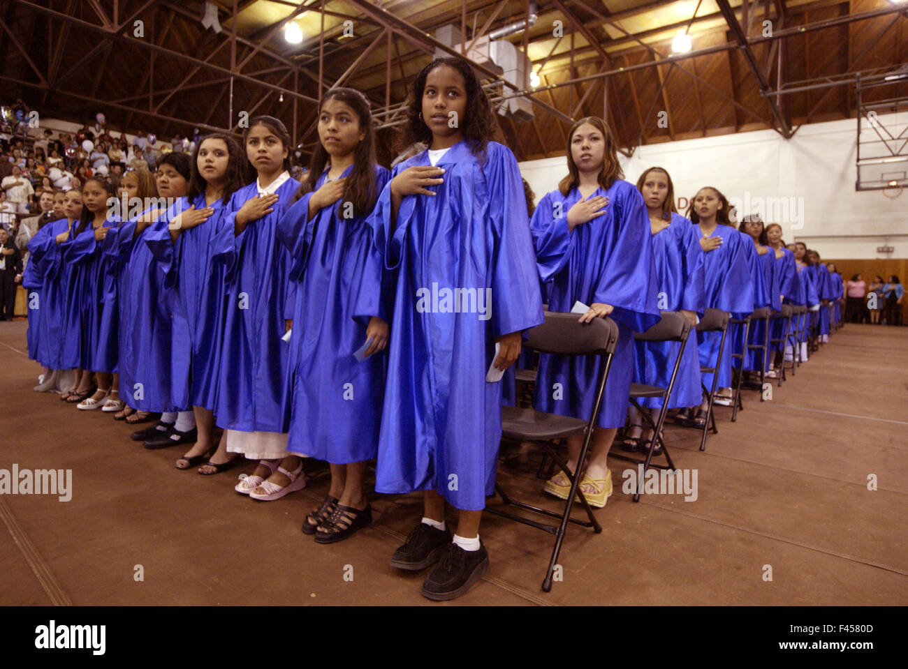 Multiethnic middle school girls wearing blue graduation gowns recite ...