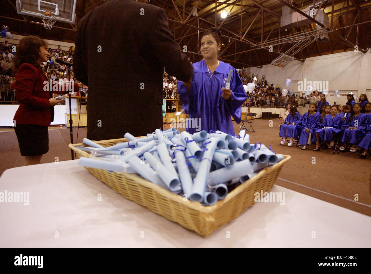 A Hispanic middle school girl wearing a blue graduation gown receives ...