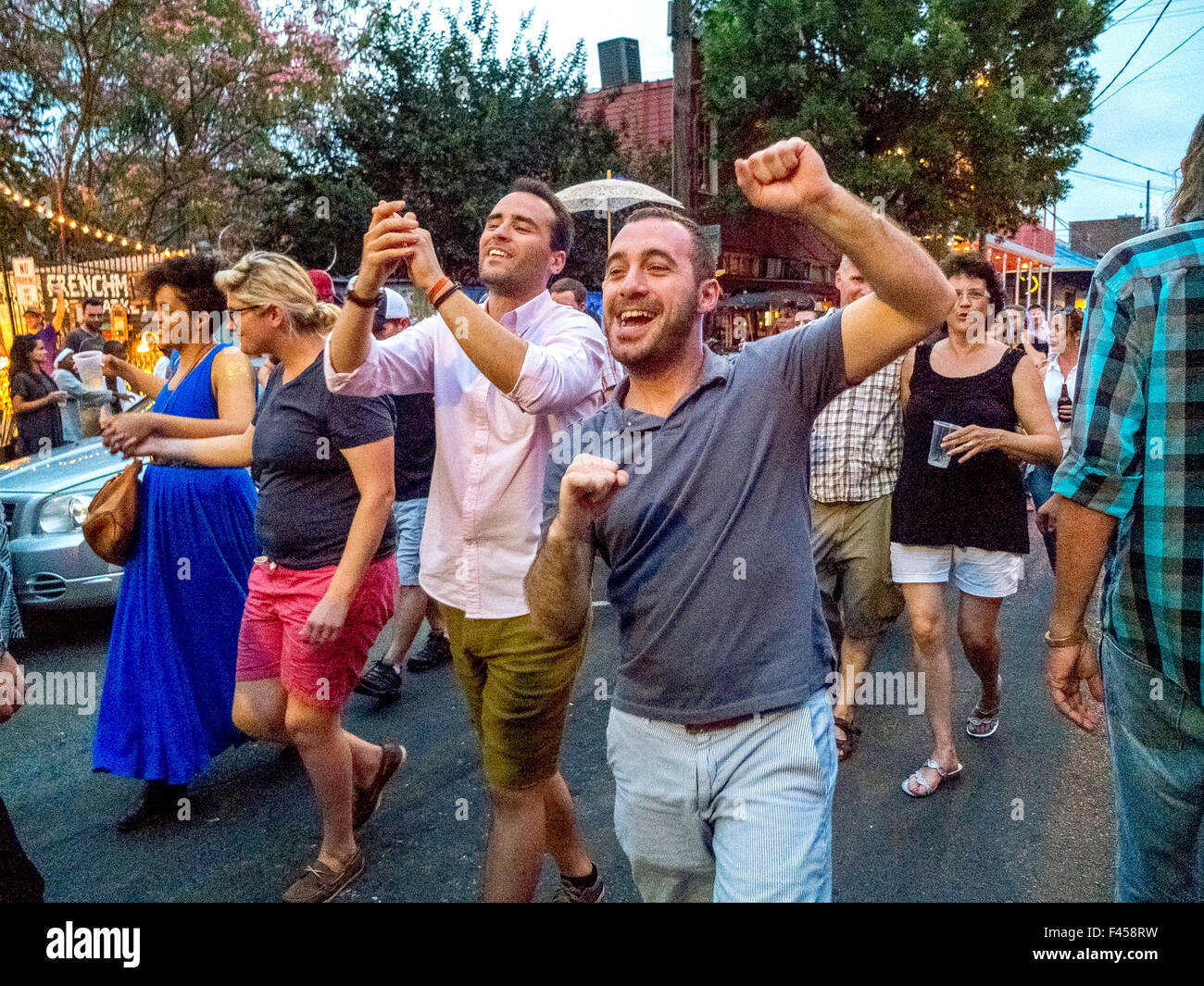 A cheering multiracial crowd follows a street band celebrating a local ...