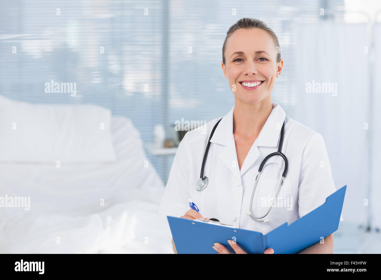 Happy doctor writing on clipboard behind bed Stock Photo - Alamy