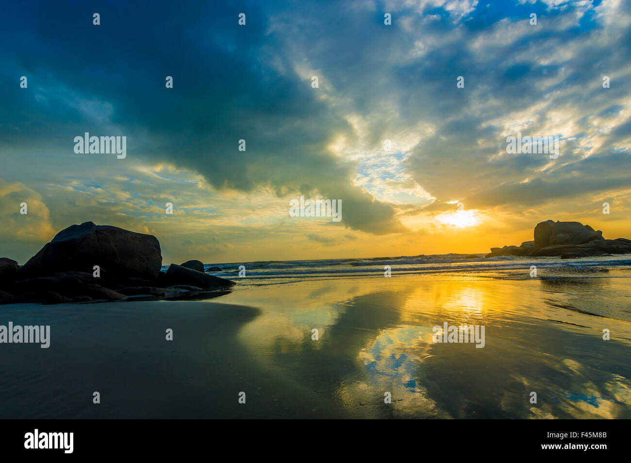 Colorful cloudy sunrise at the beach with reflection and rocks Stock ...