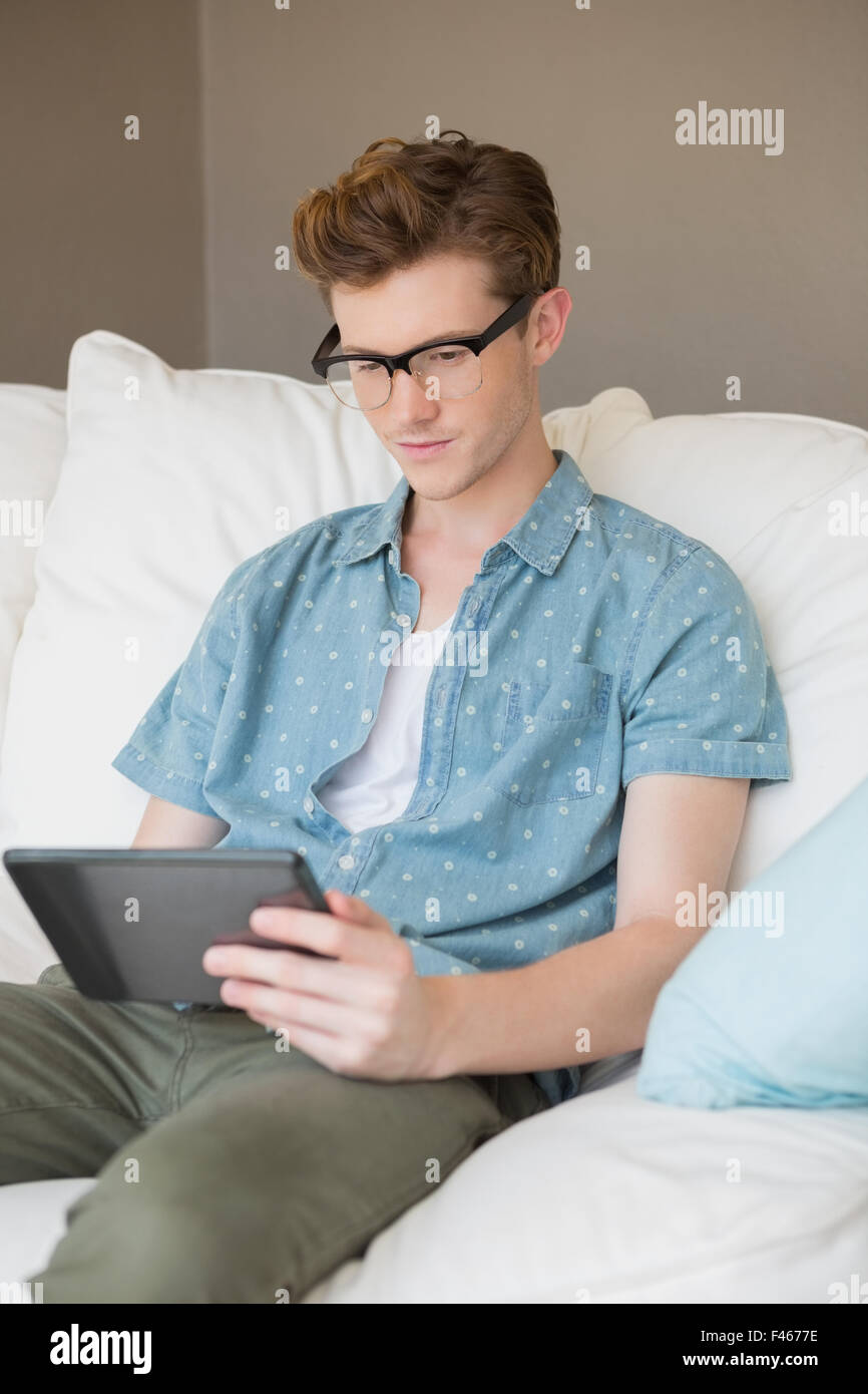 Concentrated young man using tablet on couch Stock Photo - Alamy