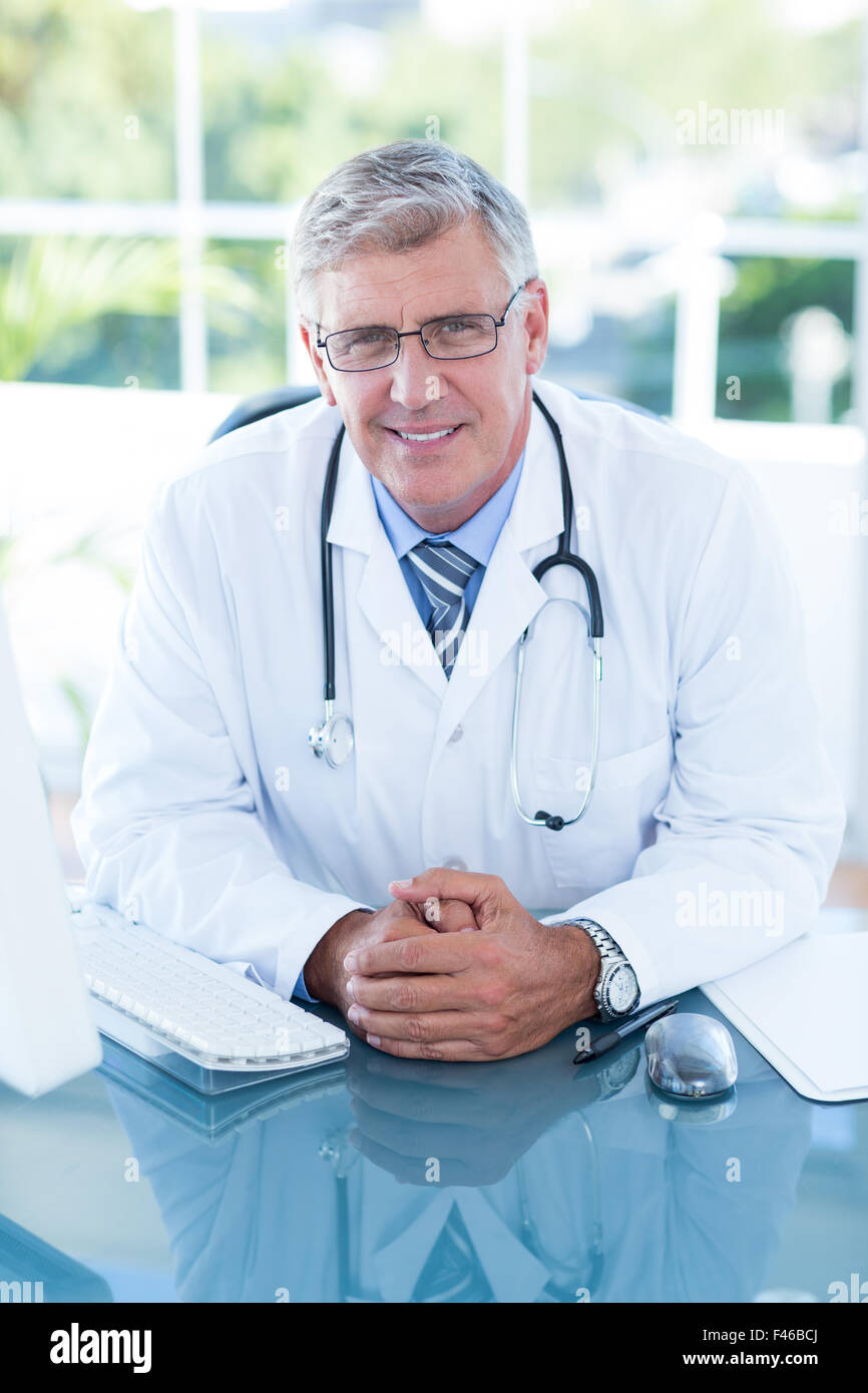 Smiling doctor sitting at his desk Stock Photo - Alamy