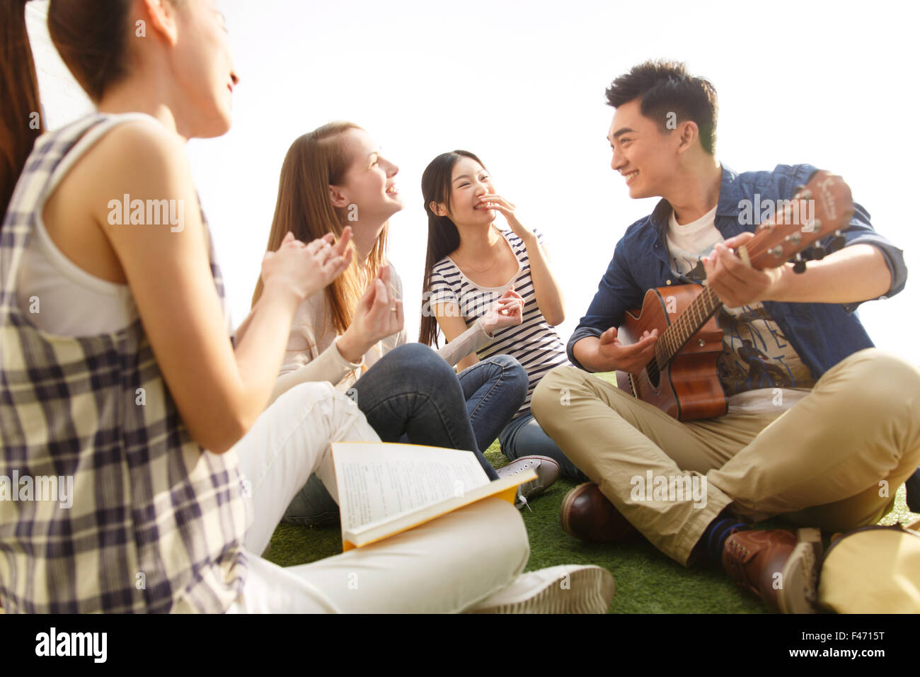 Young people sitting on lawn singing Stock Photo - Alamy
