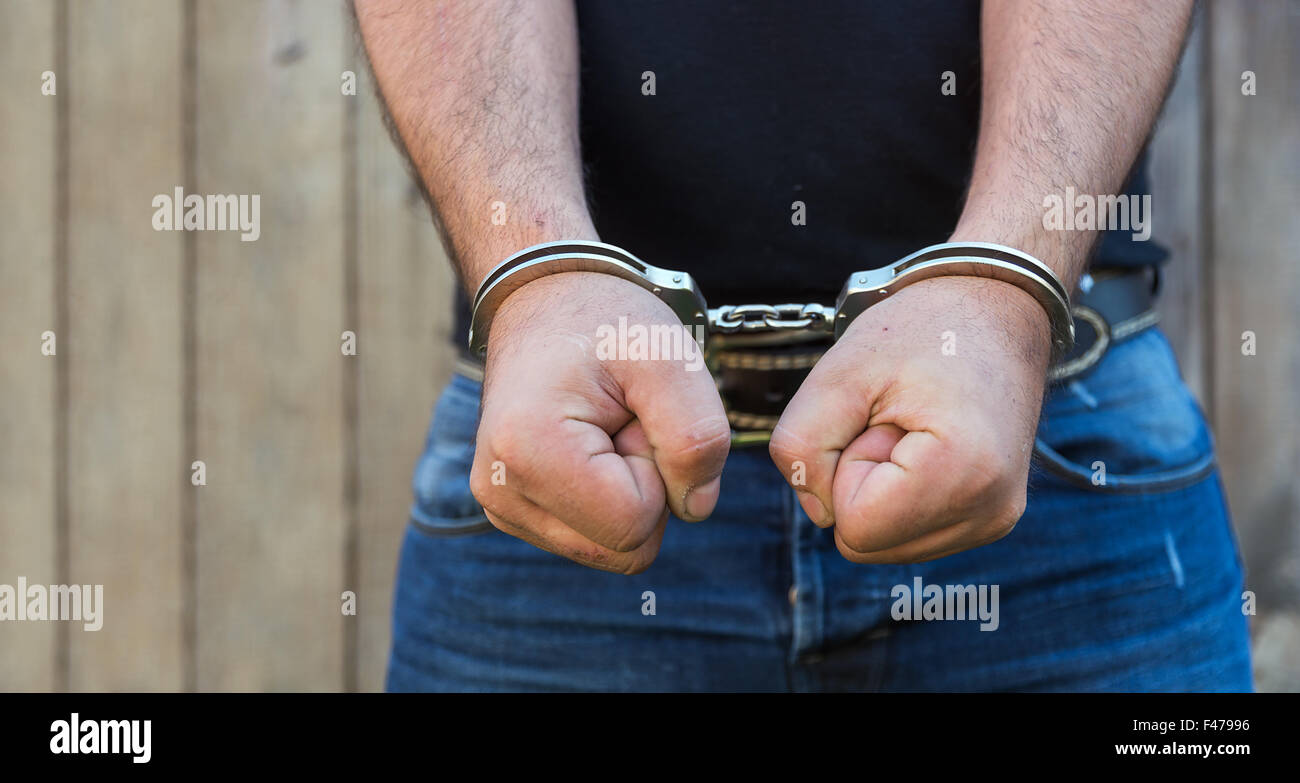 Arrest, close-up shot man's hands with handcuffs in front of plank wood ...