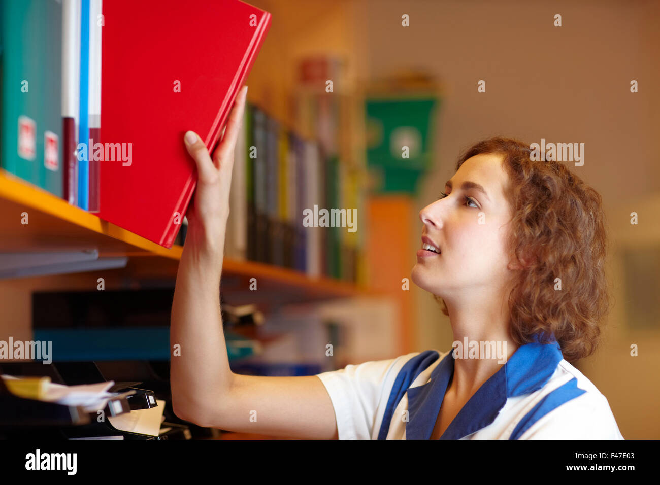 Female pharmacist taking red book from a shelf Stock Photo - Alamy