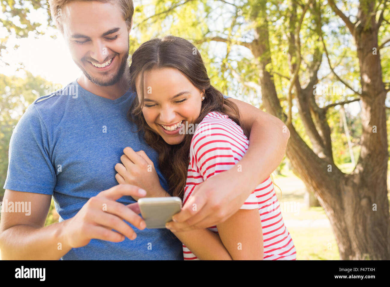 Cute couple using mobile phone in the park Stock Photo - Alamy