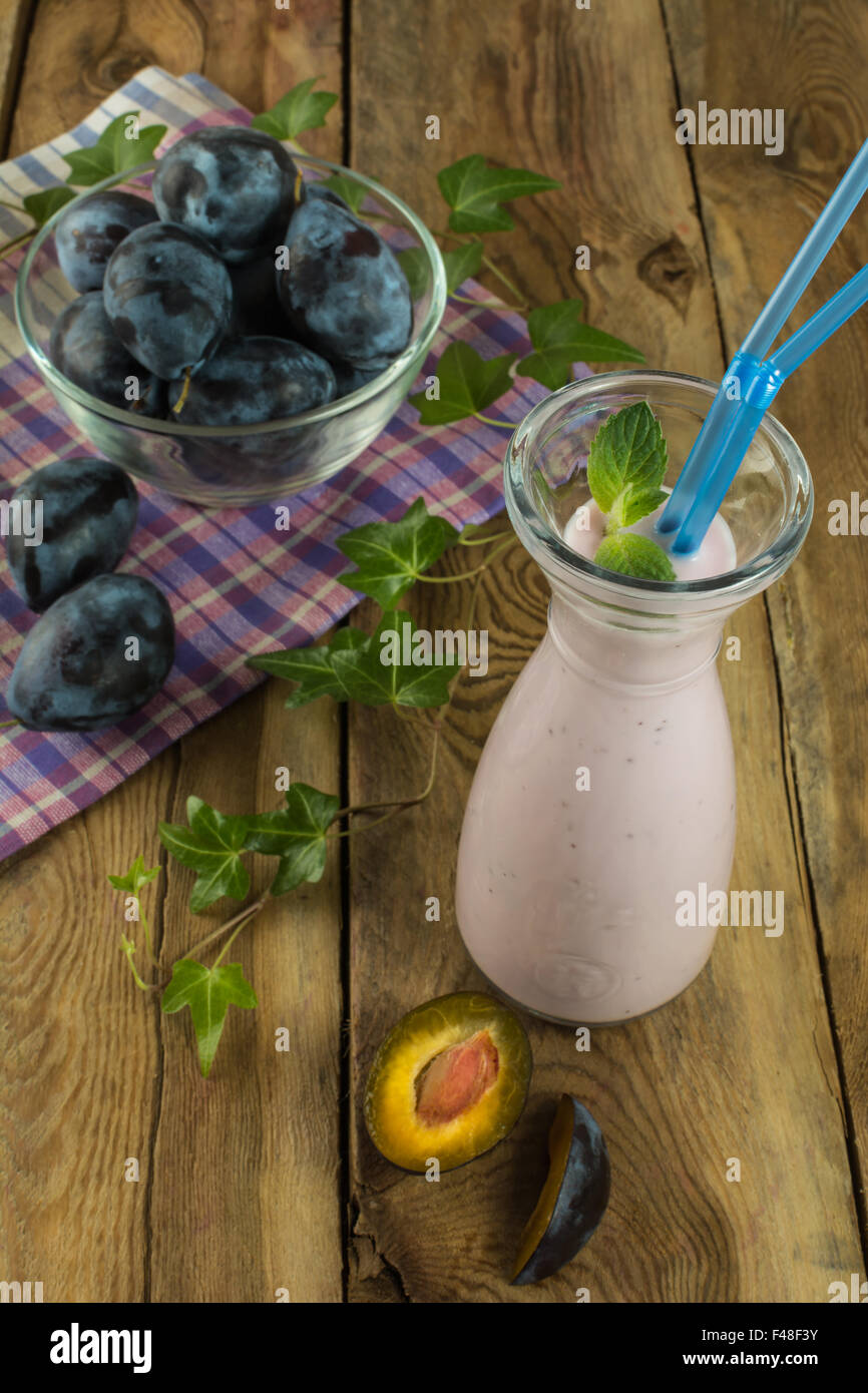 Prune drink in a glass with drinking straw plum and leaves on wooden ...