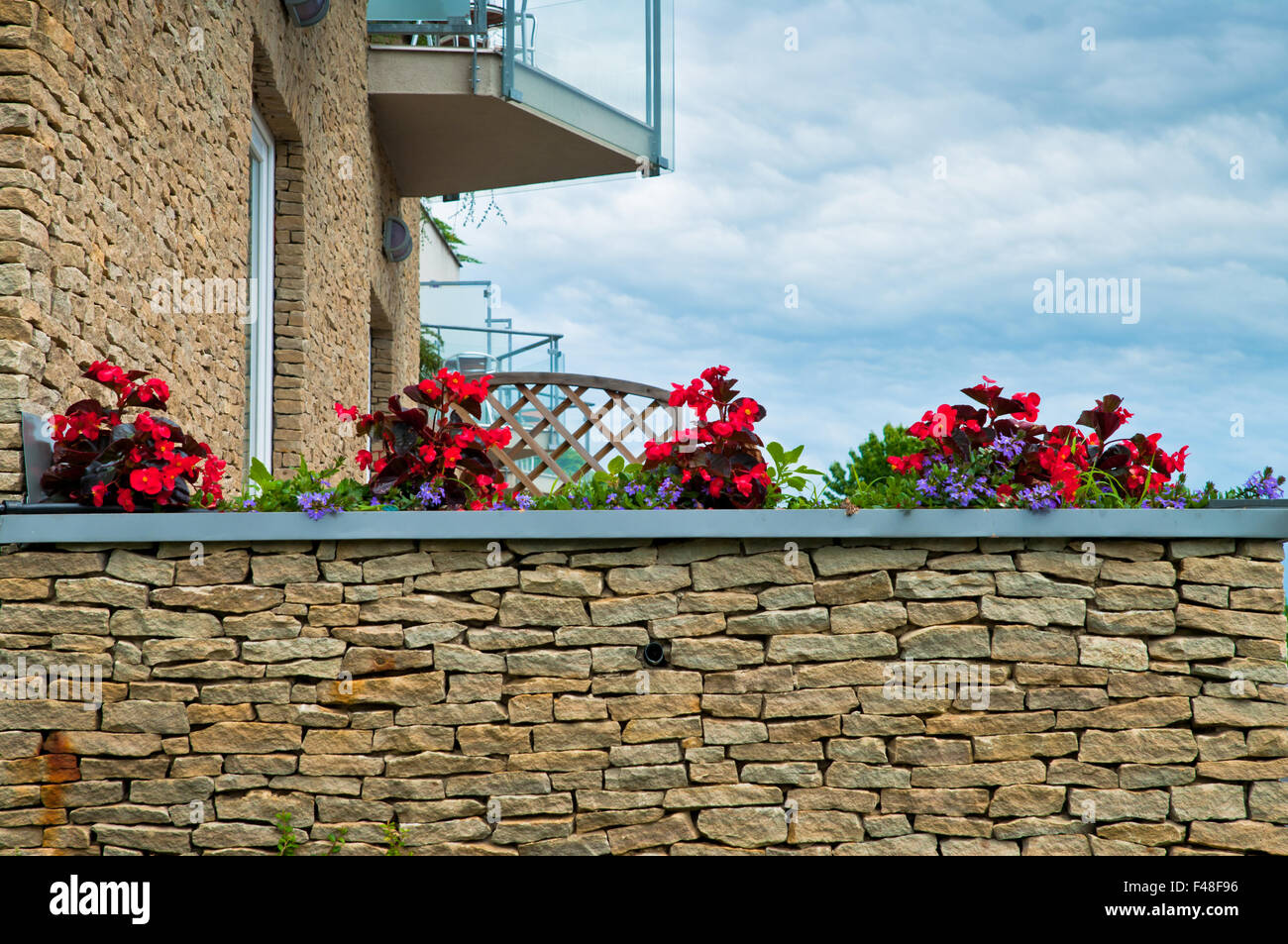 Red flowers on a balcony with modern building and cloudy sky Stock ...