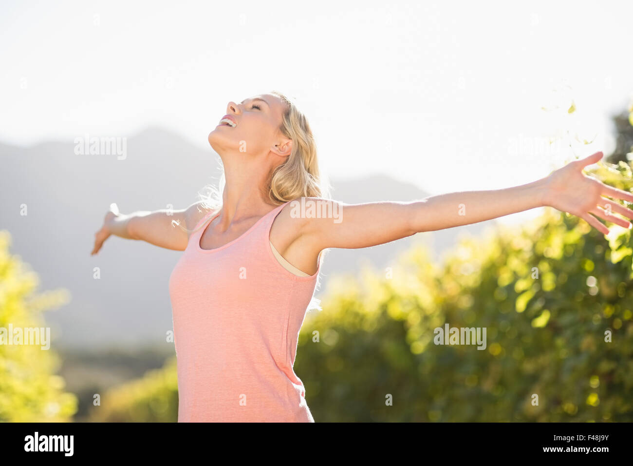 Smiling blonde woman standing in front of grapevine with eyes closed ...