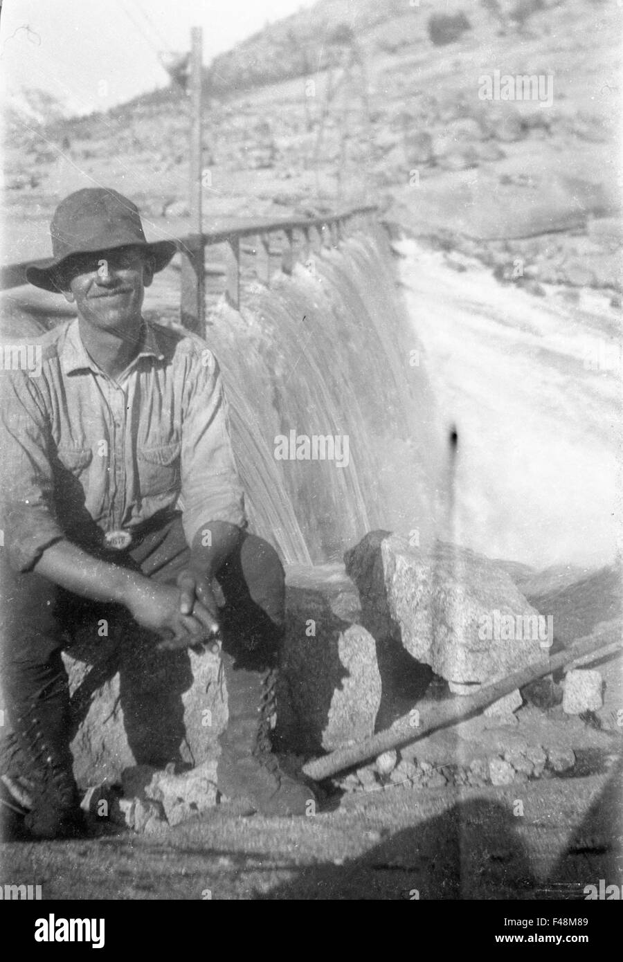 Worker in hat and boots next to dam with running water Stock Photo - Alamy