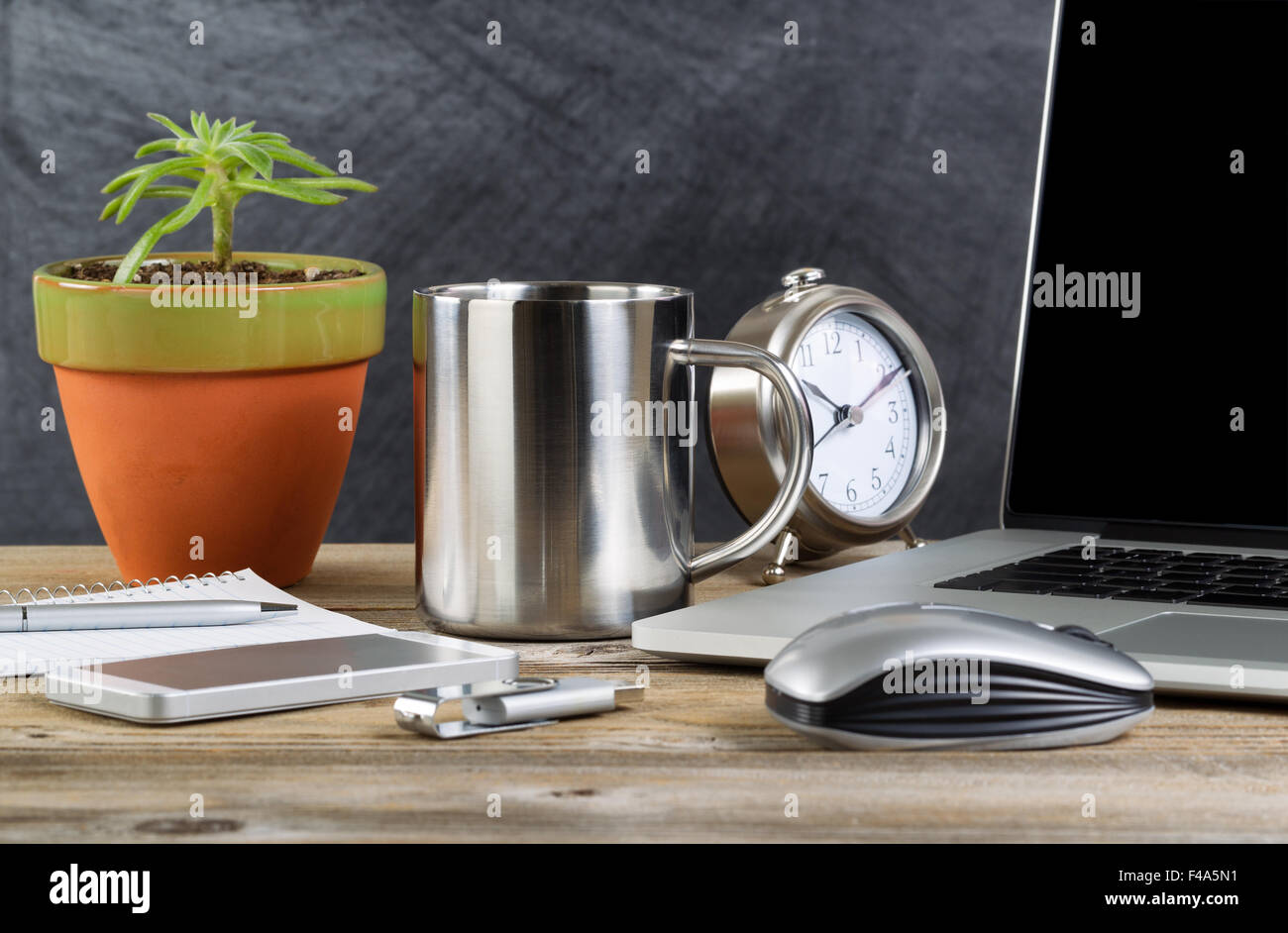 Working desktop with laptop, mouse, clock, cell phone, notebook, pen ...