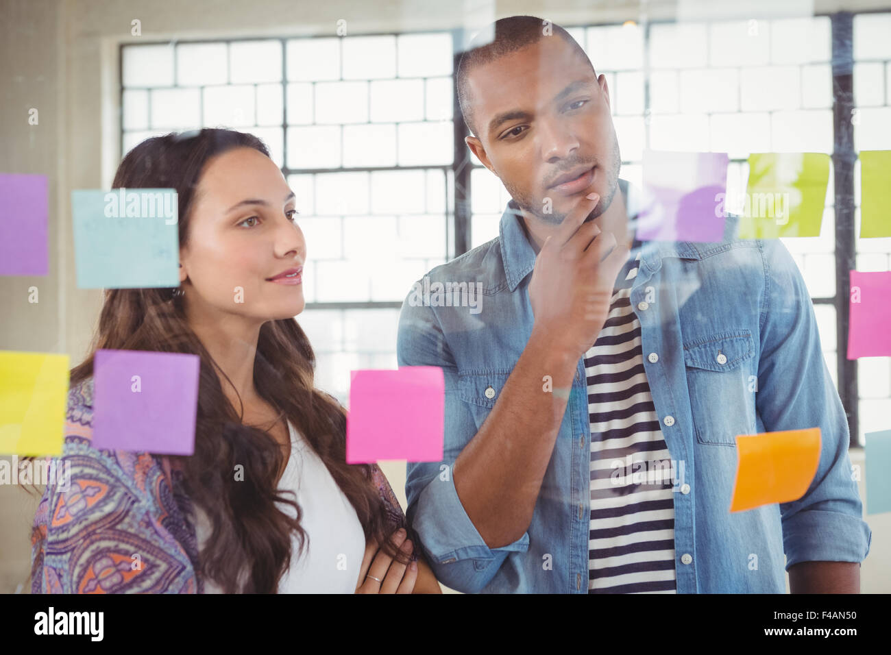 Colleagues looking at sticky notes on glass window Stock Photo - Alamy