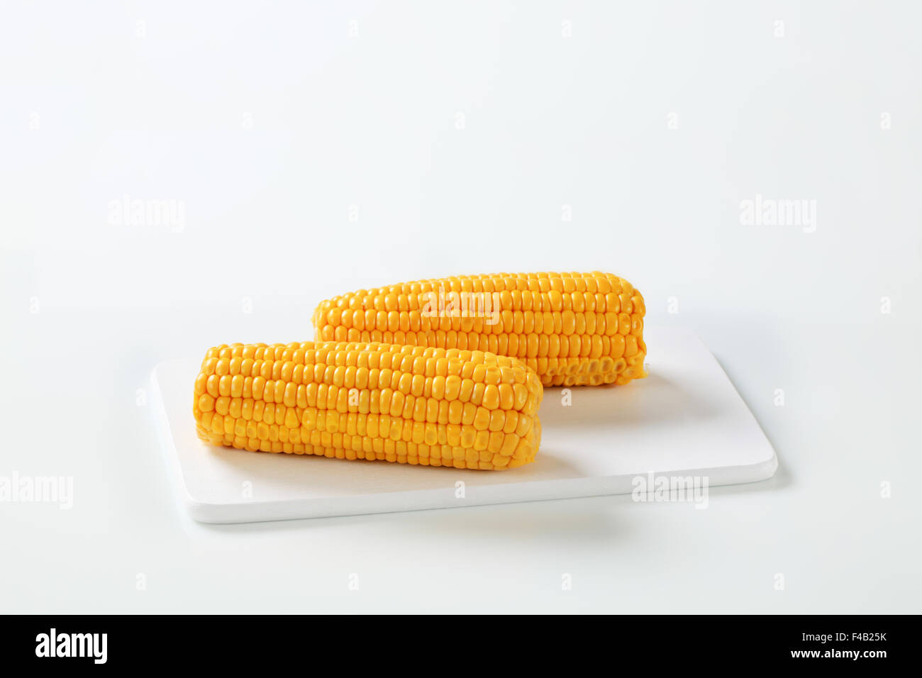 two boiled corn cobs on white cutting board Stock Photo - Alamy
