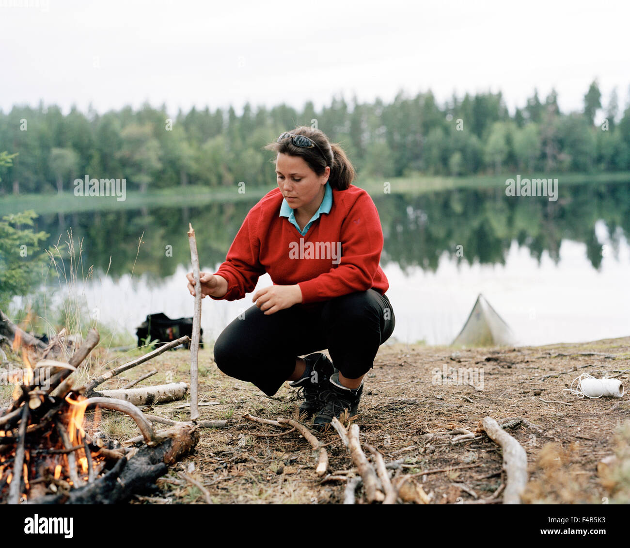 A woman making a fire by a lake Stock Photo - Alamy