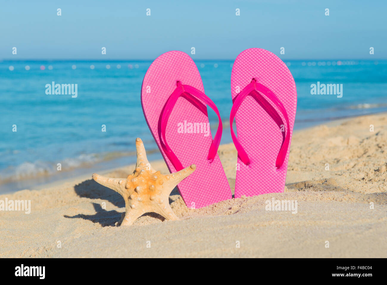 Travel by sea. Beach vacation. Pink flip-flops and starfish on sandy ...